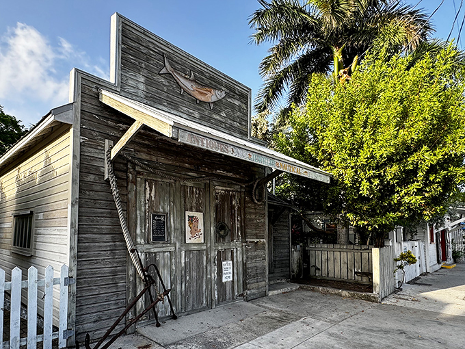 The unassuming exterior of 90 Miles To Cuba stands like a weathered sentinel of Key West history, colorful nautical flags beckoning curious travelers to explore its treasures.