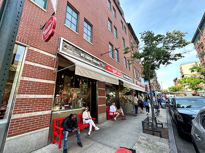 Murray's iconic storefront on Bleecker Street stands as a beacon of dairy devotion, with its signature red bench inviting cheese pilgrims to rest their weary feet before the next round.