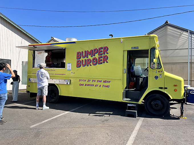 The bright yellow Bumper Burger food truck stands like a culinary lighthouse, beckoning hungry travelers under its rustic wooden shelter. Simple setting, extraordinary flavors.