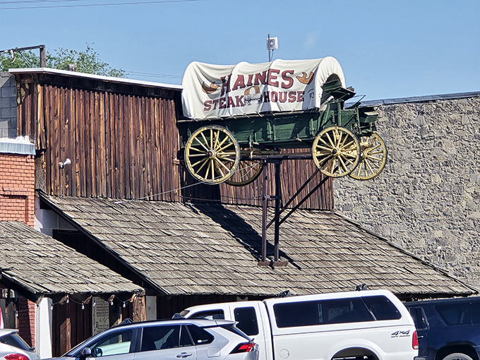 Where Western dreams meet culinary reality: The iconic covered wagon sign announces your arrival at Haines Steak House, a wooden time capsule of flavor in Eastern Oregon.