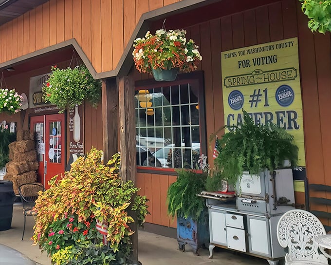The entrance to food paradise! Vibrant hanging flower baskets frame SpringHouse's rustic wooden exterior, where that milk bottle sign promises farm-fresh goodness inside.