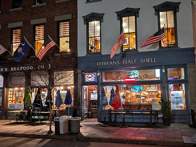 The iconic blue storefront of Hyman's glows with promise as evening falls, flags fluttering like a patriotic welcome committee for hungry visitors.