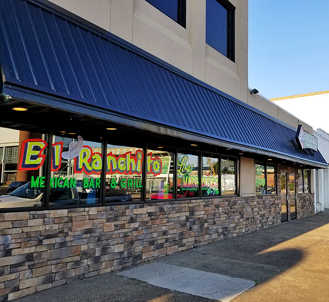 The vibrant storefront of El Ranchito glows like a beacon of culinary promise, its colorful signage and stone facade practically shouting "authentic Mexican food happens here!"