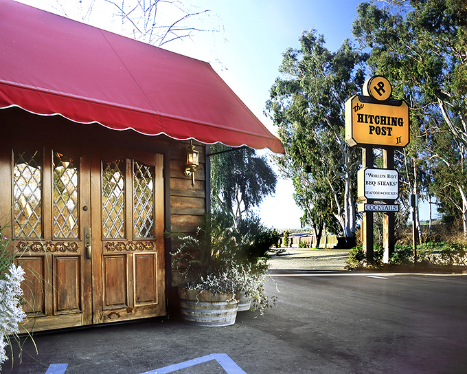The iconic red awning and rustic wooden entrance of The Hitching Post II welcomes hungry travelers like a beacon of hope for carnivores on the highway.