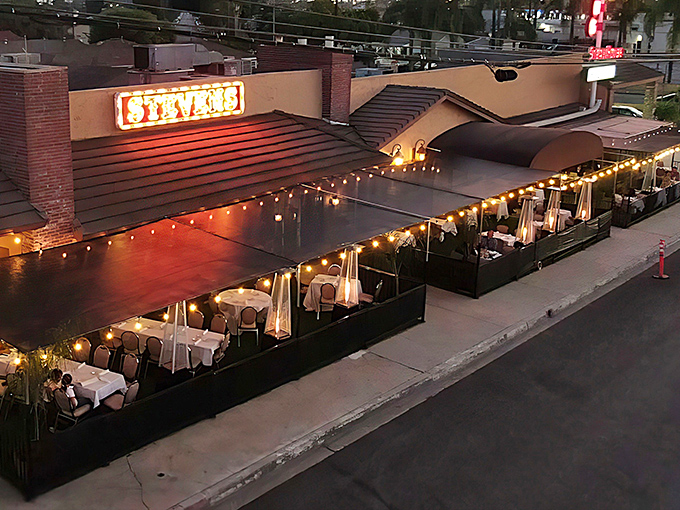 The iconic neon sign beckons hungry travelers like a lighthouse for carnivores, while the outdoor patio promises an evening of culinary magic under twinkling lights.
