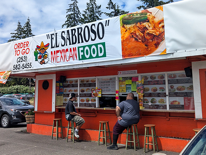 The red-roofed taqueria stands out like a culinary lighthouse, beckoning hungry travelers with its vibrant orange walls and festive papel picado banners.