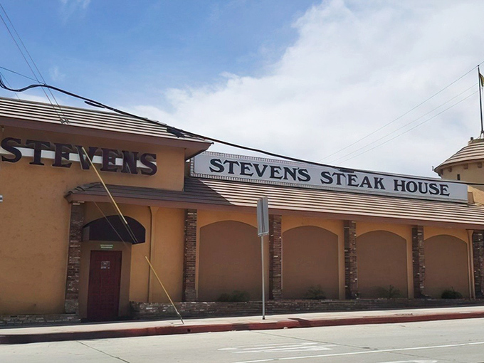 The iconic neon sign beckons hungry travelers like a lighthouse for carnivores, while the outdoor patio promises an evening of culinary magic under twinkling lights.