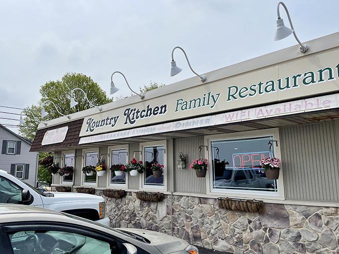 The unassuming exterior of Kountry Kitchen Family Restaurant, where hanging flower baskets and stone foundation hint at the homey comfort waiting inside.