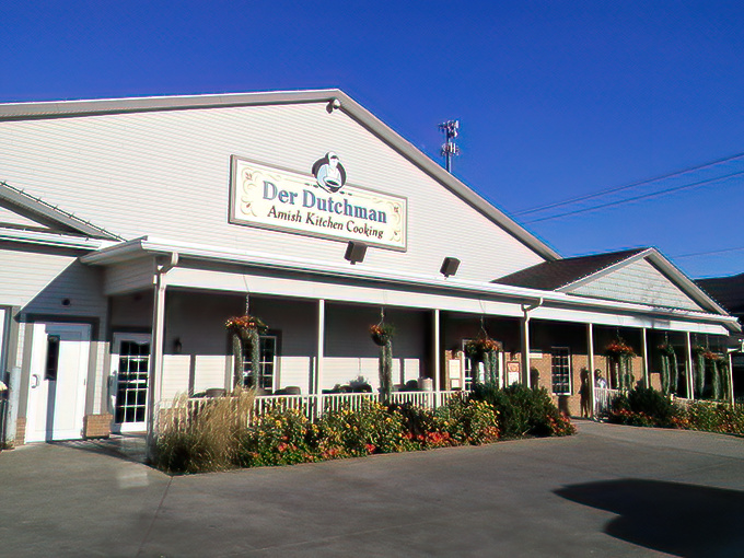 The welcoming white exterior of Der Dutchman stands like a beacon of comfort food in Walnut Creek, where hanging flower baskets add splashes of color to Amish simplicity.