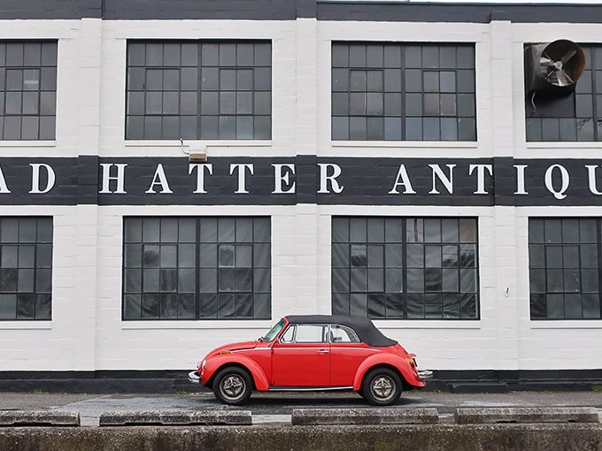 The white facade of Mad Hatter Antiques stands like a portal to the past, with blue "OPEN" flags beckoning treasure hunters to step inside and explore.