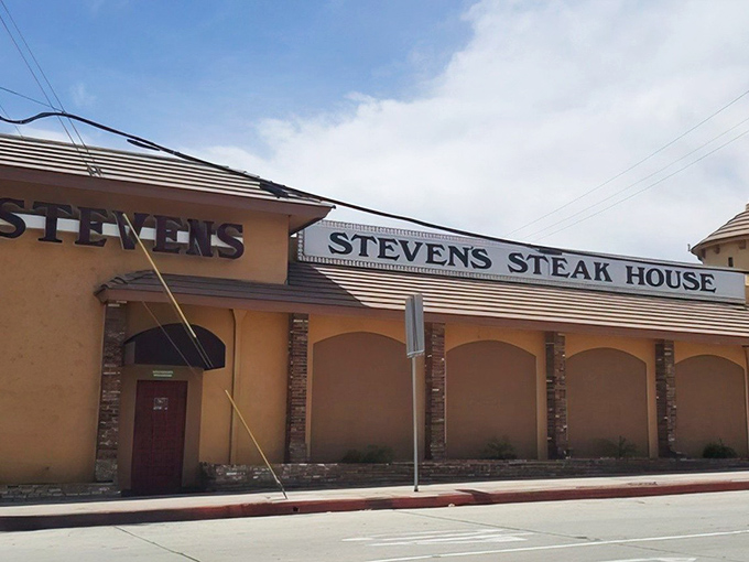 The iconic neon sign beckons hungry travelers like a lighthouse for carnivores, while the outdoor patio promises an evening of culinary magic under twinkling lights.
