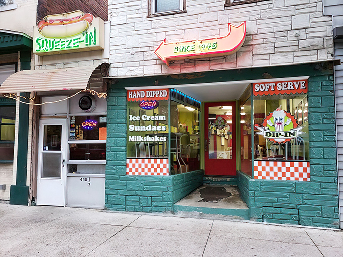 The iconic neon hot dog sign beckons hungry travelers like a culinary lighthouse. The Squeeze-In's teal facade and red awning promise unpretentious delights within.