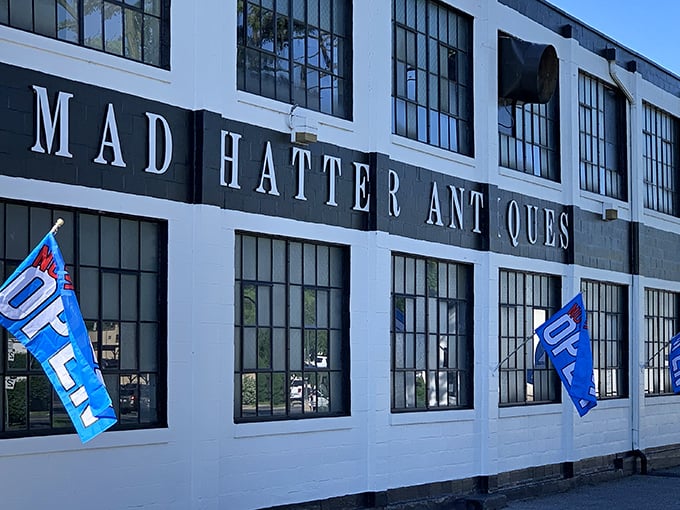 The white facade of Mad Hatter Antiques stands like a portal to the past, with blue "OPEN" flags beckoning treasure hunters to step inside and explore.