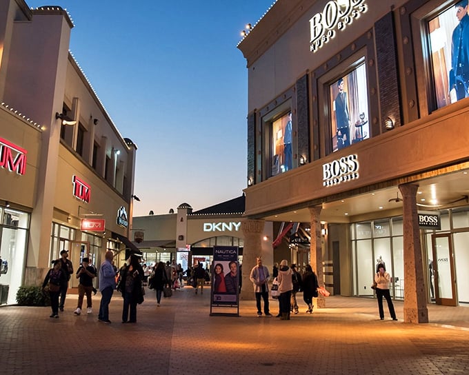 The iconic Coach store stands as a blue beacon of hope for bargain hunters, palm trees swaying as shoppers navigate their retail pilgrimage.