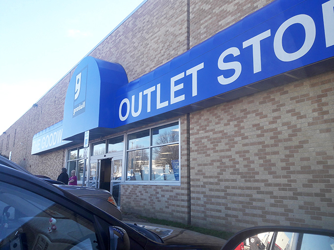 The blue Goodwill sign beckons like a lighthouse to bargain hunters navigating the seas of retail markup. Behind these doors, treasure awaits.