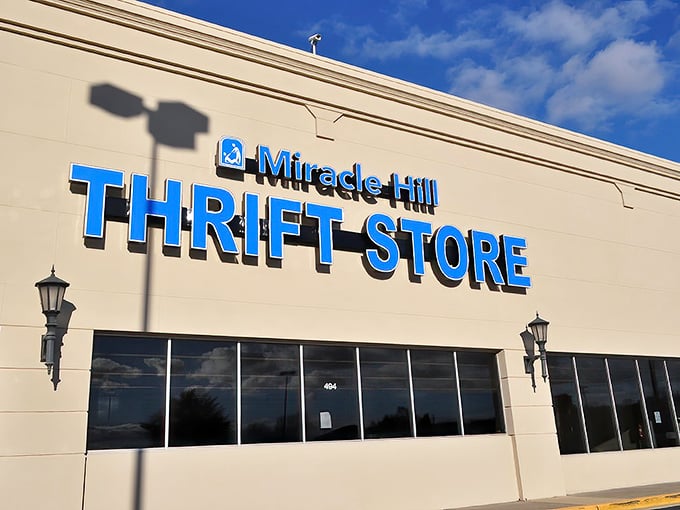 The iconic blue signage of Miracle Hill Thrift Store stands out against the beige building like a beacon for bargain hunters across Greenville.