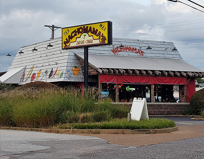 The vibrant exterior of Nachomama's beckons with colorful pepper artwork and inviting picnic tables. Tex-Mex paradise awaits behind that neon glow.