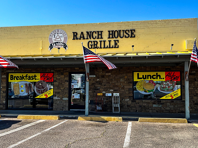 The unassuming exterior of Ranch House Grille, where American flags flutter in welcome and palm trees stand guard over breakfast paradise.