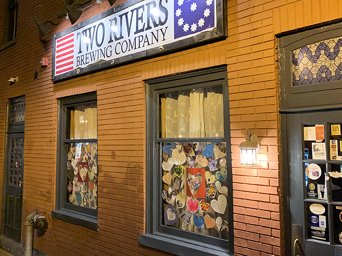 The historic brick facade of Two Rivers Brewing Company glows with warmth, its American flag-inspired sign beckoning hungry travelers like a culinary lighthouse.
