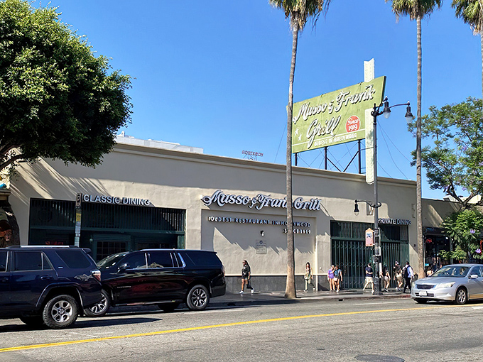 The iconic green and red sign of Musso & Frank stands proudly on Hollywood Boulevard, a beacon of culinary history amid the palm trees.