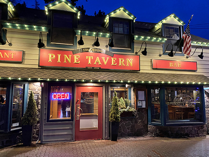 The charming exterior of Pine Tavern beckons with its classic red awning and stone facade, a timeless landmark in downtown Bend since the Great Depression era.