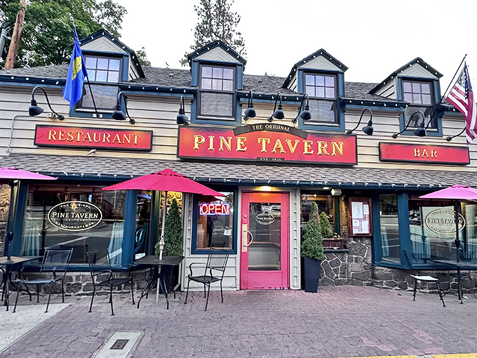 The charming exterior of Pine Tavern beckons with its classic red awning and stone facade, a timeless landmark in downtown Bend since the Great Depression era.