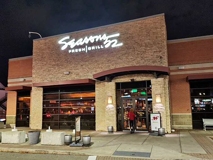 The stone facade of Seasons 52 stands like a culinary lighthouse, beckoning hungry travelers with its warm glow and those unmistakable bright green umbrellas.