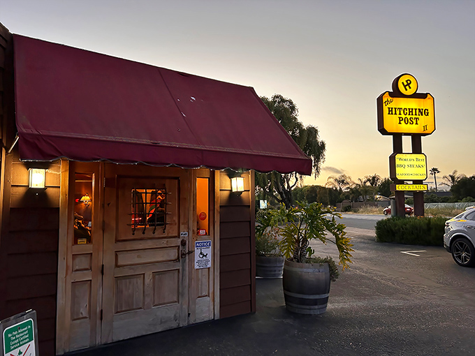 The iconic red awning and rustic wooden entrance of The Hitching Post II welcomes hungry travelers like a beacon of hope for carnivores on the highway.