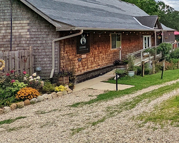 The rustic cedar-shingled exterior of Ugly Bunny Winery welcomes visitors with colorful flower gardens and a gravel path that whispers, "Slow down, you've arrived."