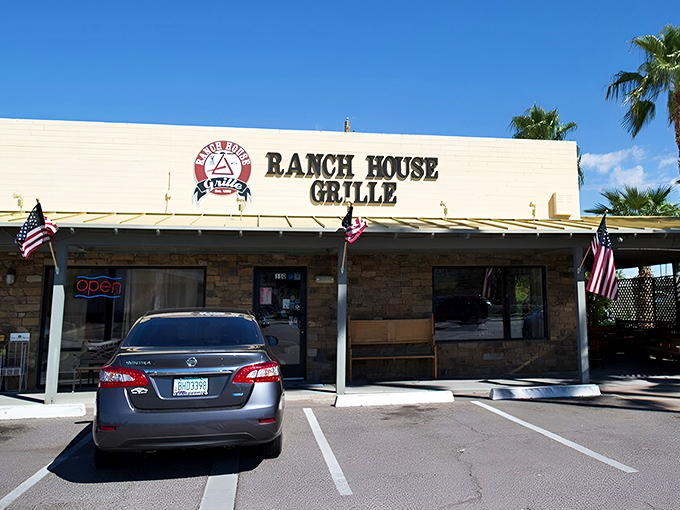 The unassuming exterior of Ranch House Grille, where American flags flutter in welcome and palm trees stand guard over breakfast paradise.
