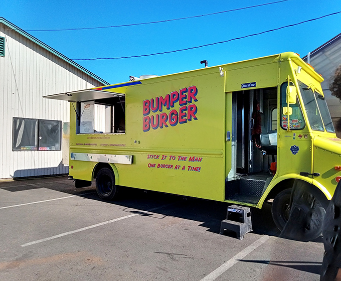 The bright yellow Bumper Burger food truck stands like a culinary lighthouse, beckoning hungry travelers under its rustic wooden shelter. Simple setting, extraordinary flavors.