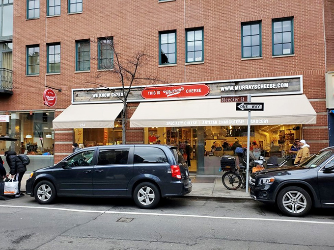 Murray's iconic storefront on Bleecker Street stands as a beacon of dairy devotion, with its signature red bench inviting cheese pilgrims to rest their weary feet before the next round.