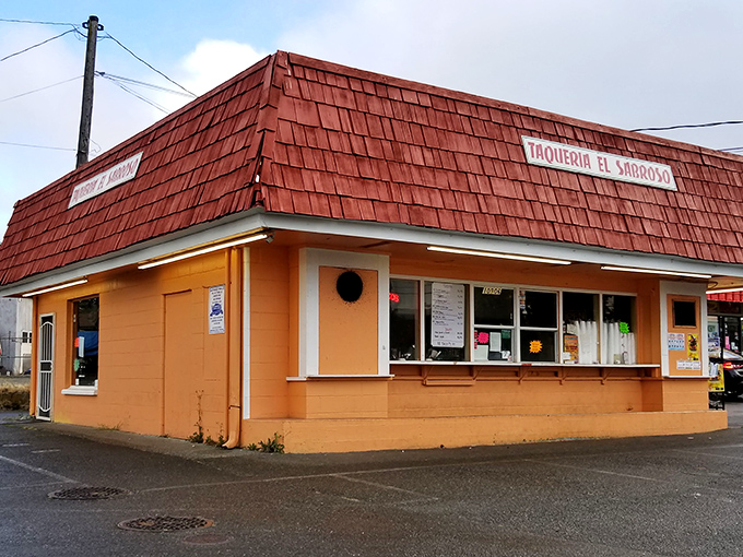 The red-roofed taqueria stands out like a culinary lighthouse, beckoning hungry travelers with its vibrant orange walls and festive papel picado banners.