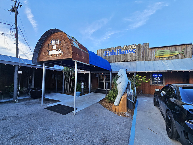 The weathered wooden exterior of The Old Fish House screams "authentic Florida" with its blue signage and that charming manatee statue standing guard at the entrance.