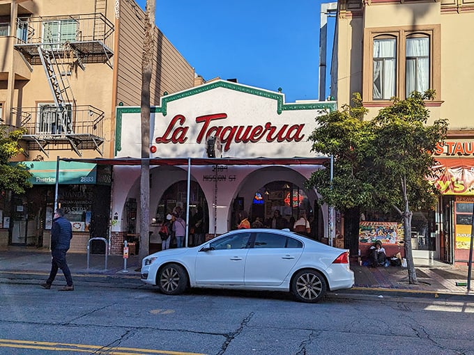 The iconic white facade with that bold red script is like a beacon for burrito pilgrims. La Taqueria's exterior promises culinary magic within those arched entryways.