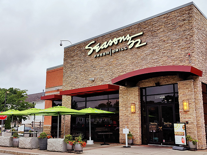 The stone facade of Seasons 52 stands like a culinary lighthouse, beckoning hungry travelers with its warm glow and those unmistakable bright green umbrellas.