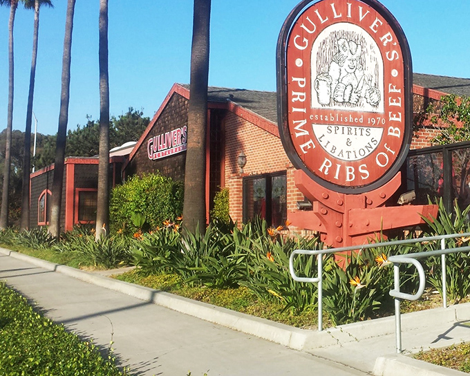 The iconic red sign beckons like a lighthouse for meat lovers. Palm trees and brick exterior create that perfect California-meets-Old-England vibe.