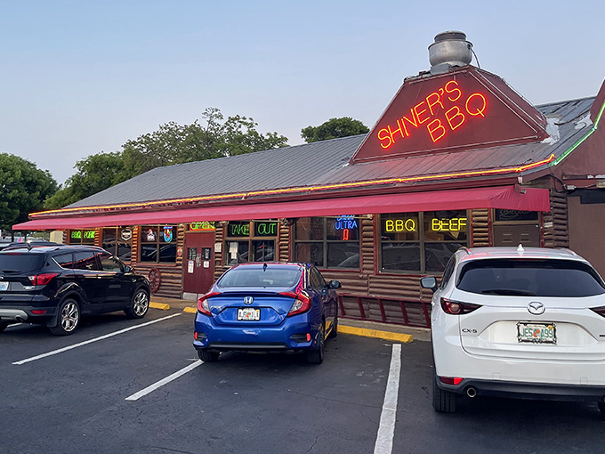 That neon sign isn't just advertising &ndash; it's a lighthouse for hungry souls. The log cabin exterior promises authentic barbecue without pretension.