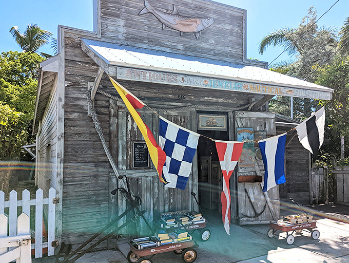 The unassuming exterior of 90 Miles To Cuba stands like a weathered sentinel of Key West history, colorful nautical flags beckoning curious travelers to explore its treasures.