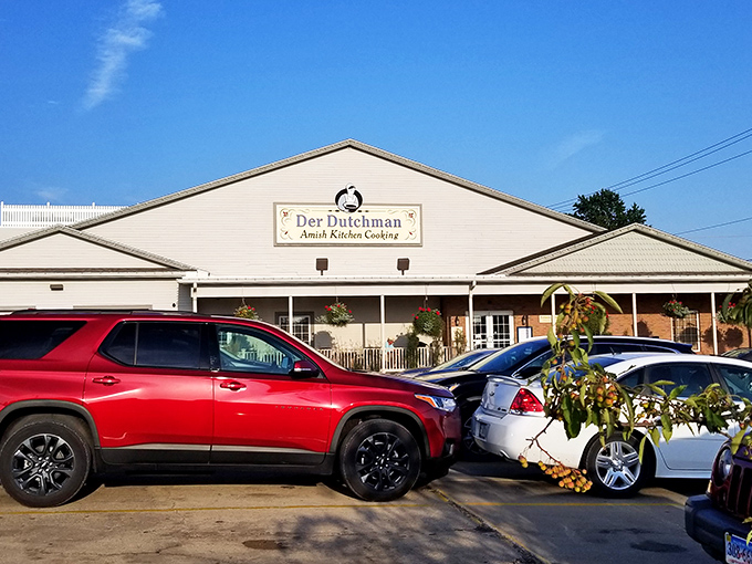 The welcoming white exterior of Der Dutchman stands like a beacon of comfort food in Walnut Creek, where hanging flower baskets add splashes of color to Amish simplicity.