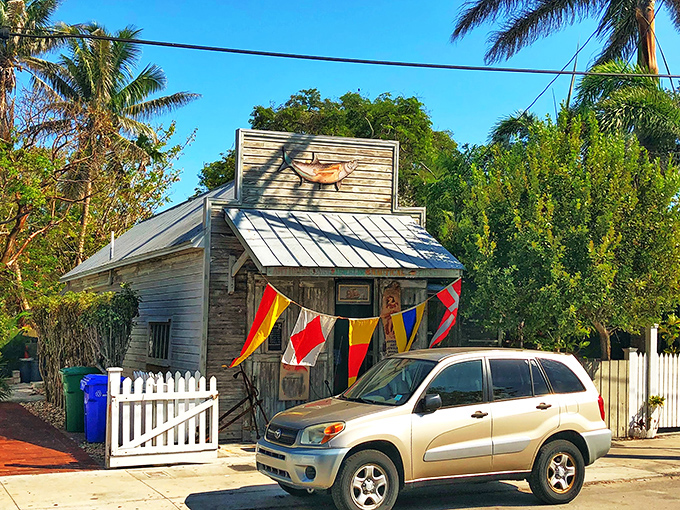 The unassuming exterior of 90 Miles To Cuba stands like a weathered sentinel of Key West history, colorful nautical flags beckoning curious travelers to explore its treasures.