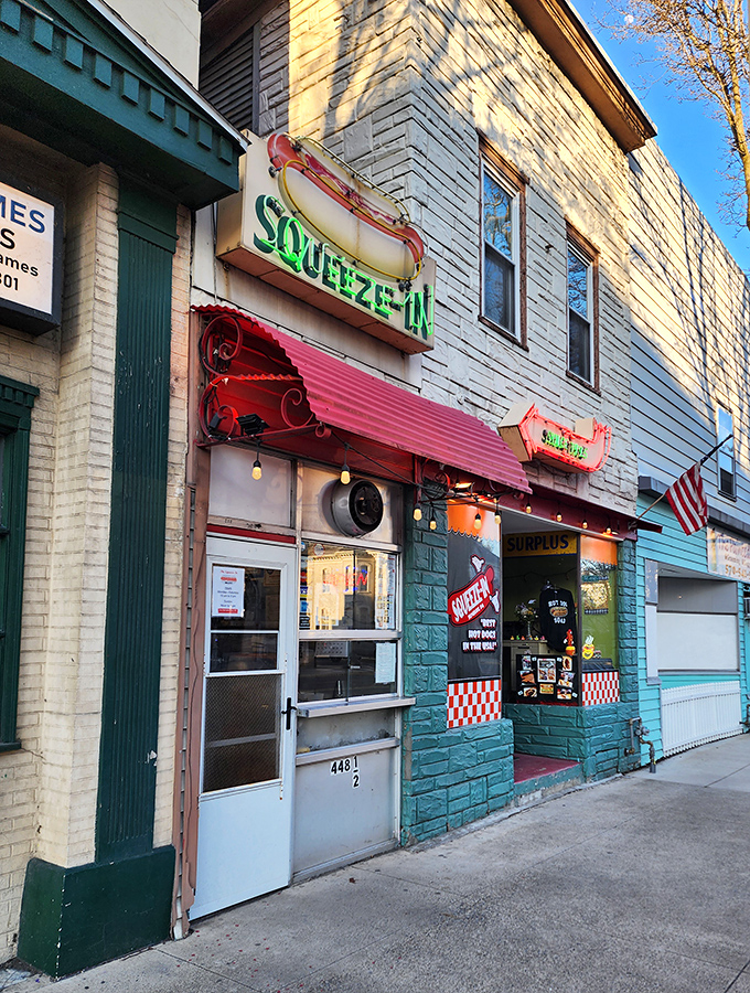 The iconic neon hot dog sign beckons hungry travelers like a culinary lighthouse. The Squeeze-In's teal facade and red awning promise unpretentious delights within.