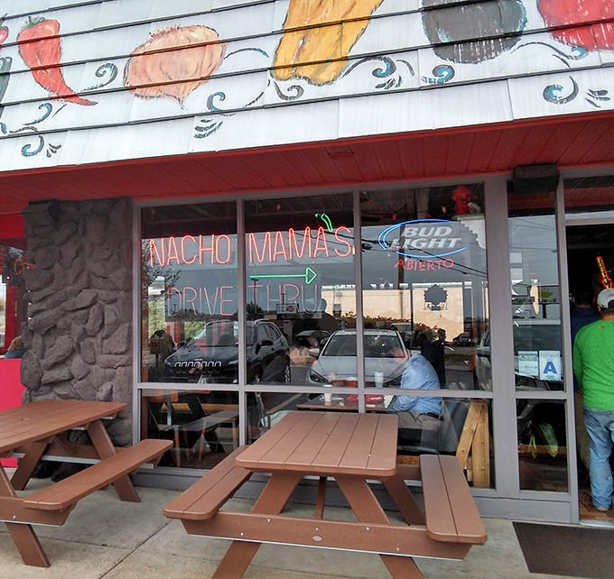 The vibrant exterior of Nachomama's beckons with colorful pepper artwork and inviting picnic tables. Tex-Mex paradise awaits behind that neon glow.