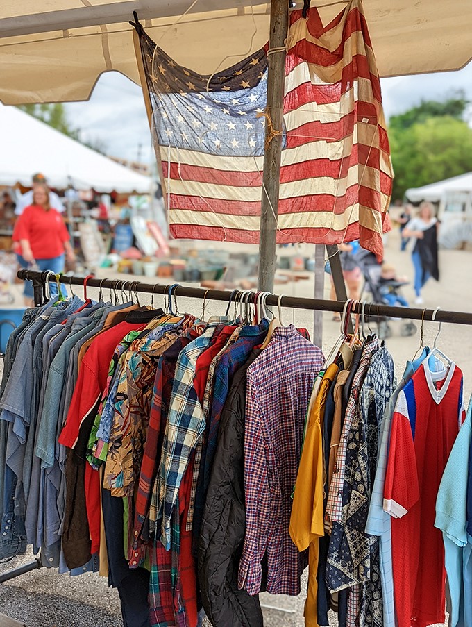 Vintage clothing waits for its next chapter under weathered American flags&mdash;patriotism and fashion in perfect, sun-dappled harmony.