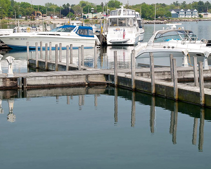 Marina slips mirror the boats they cradle, creating perfect symmetry on calm waters. Lake Huron's playground for those who hear water's call.