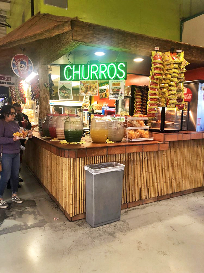 The churro stand's neon glow is the marketplace's North Star, with fruit aguas frescas in rainbow hues standing ready to cool spice-tingled taste buds.