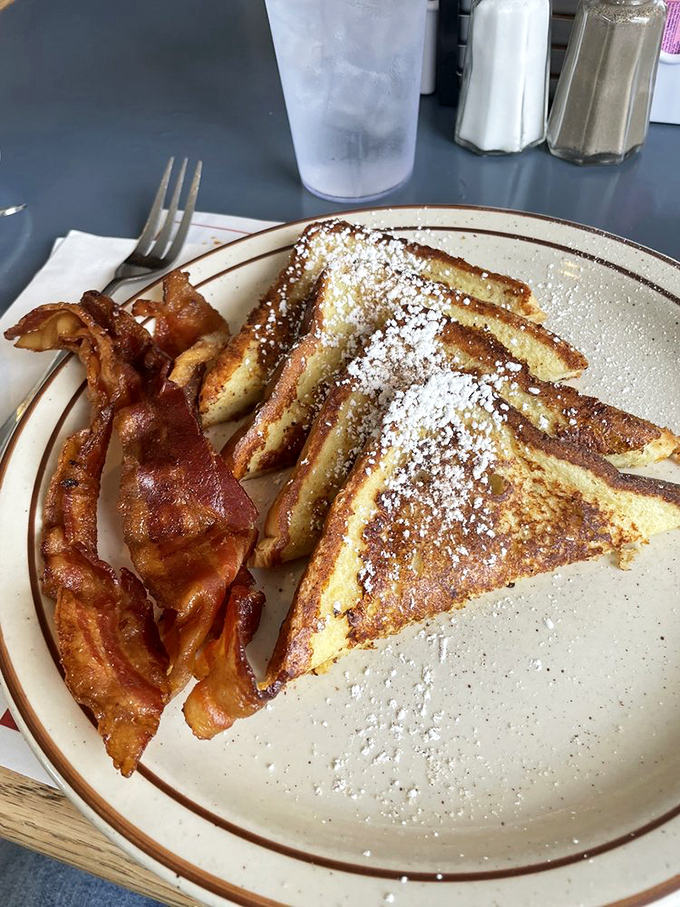 French toast dusted with powdered sugar like a winter morning, alongside bacon that's achieved that perfect crispy-chewy harmony.