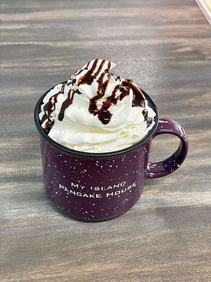 Hot chocolate that's more cloud than beverage, topped with a mountain of whipped cream and chocolate drizzle in their signature speckled mug.