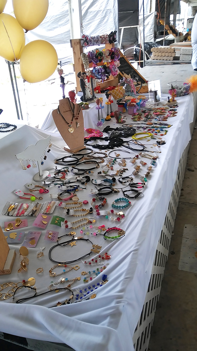 A universe of handcrafted jewelry spreads across white tablecloths like a constellation of possibilities, each piece waiting for its perfect match. 