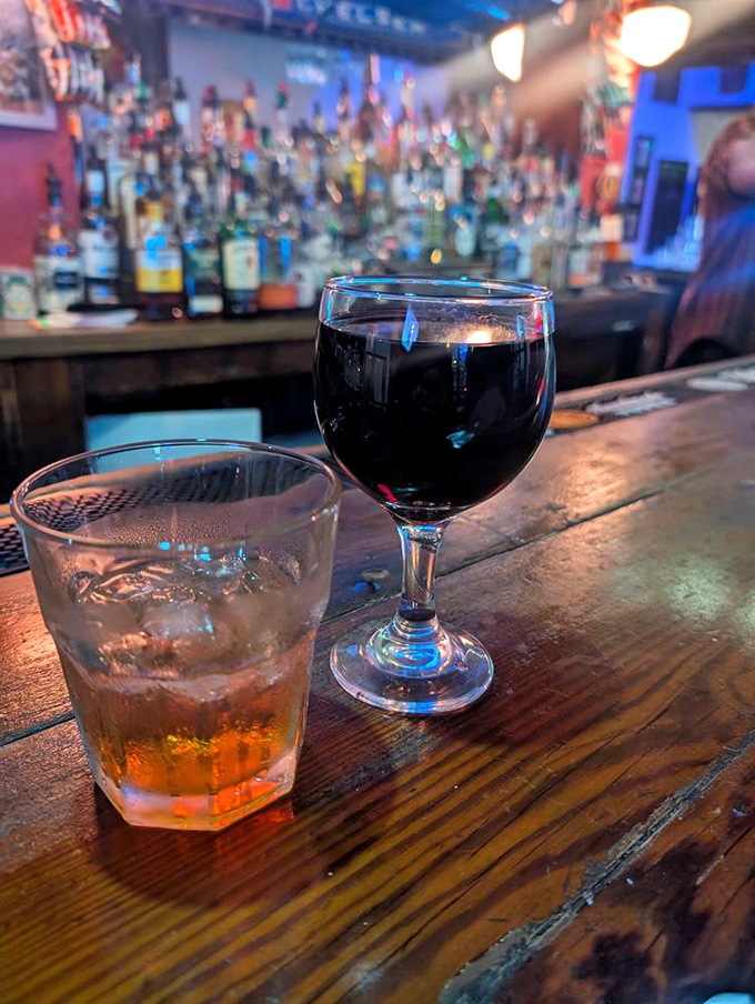 Two glasses, infinite possibilities. The amber whiskey and ruby wine sitting on that weathered wood bar represent the beginning of many great New Orleans stories.